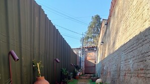 Um caminho estreito com pedras para pisar, serpenteando por um jardim com plantas em vasos e uma parede de tijolos ao lado.