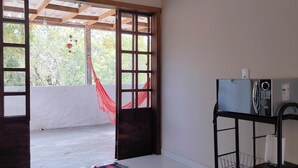 Quarto com uma porta grande aberta para área externa, ventilador de teto, micro-ondas em carrinho e rede vermelha.