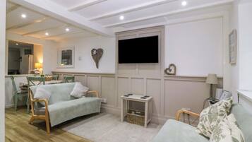 Uma sala de estar com sofá, uma mesinha, televisão e janela.