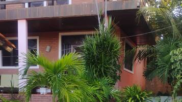 Piscina com deck de madeira, rodeada por plantas em vasos e um edifício com varanda.