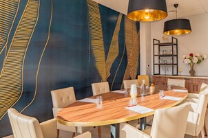 Uma área de jantar moderna com uma mesa redonda de madeira, cadeiras estofadas brancas e uma parede decorativa com padrões abstratos.