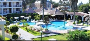 Resort com piscina central, espreguiçadeiras e palmeiras.