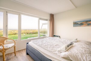 Quarto com uma janela grande, uma cama, uma cadeira e um quadro na parede.