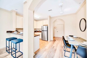 Uma cozinha moderna com uma ilha central, banquetas, uma mesa de jantar com cadeiras e uma geladeira.