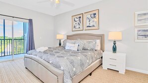 Um quarto com uma cama, duas mesas de cabeceira, um ventilador de teto e obras de arte nas paredes.