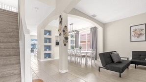 Uma sala de estar ampla com uma escada, uma mesa de jantar com cadeiras, um sofá e um quadro na parede.