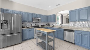 Uma cozinha moderna com eletrodomésticos de aço inoxidável, armários azuis e uma mesa de madeira.