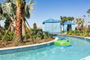 Uma piscina com boia verde insuflável, palmeiras e toldos listrados de azul.