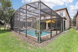 Piscina coberta com estrutura de vidro, rodeada por um gramado e uma casa ao fundo.