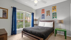 Quarto com uma janela grande, uma cama com cabeceira, duas mesas de cabeceira e um ventilador de teto.