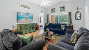 Uma sala de estar com uma televisão grande, um sofá azul, um armário verde e um ventilador de teto.