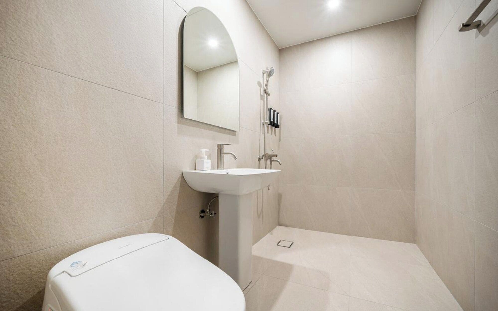 Uma casa de banho moderna com uma pia branca, espelho e chuveiro.