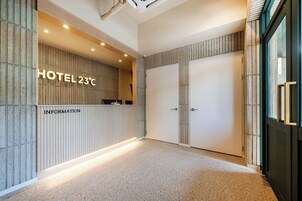 Uma área de recepção de hotel, com balcão de atendimento, indicador de temperatura e uma porta fechada.