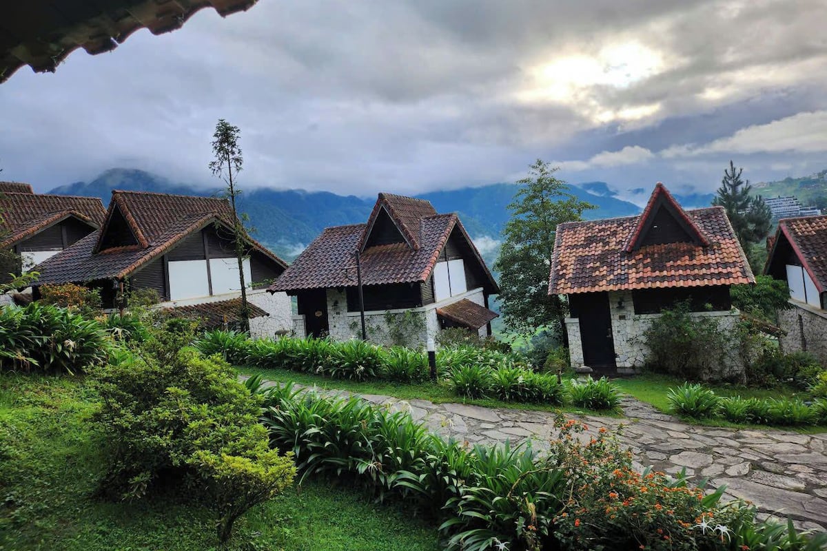 Uma fileira de casas tradicionais com telhados de azulejos e paredes de pedra, cercada por vegetação exuberante e um caminho de pedra.