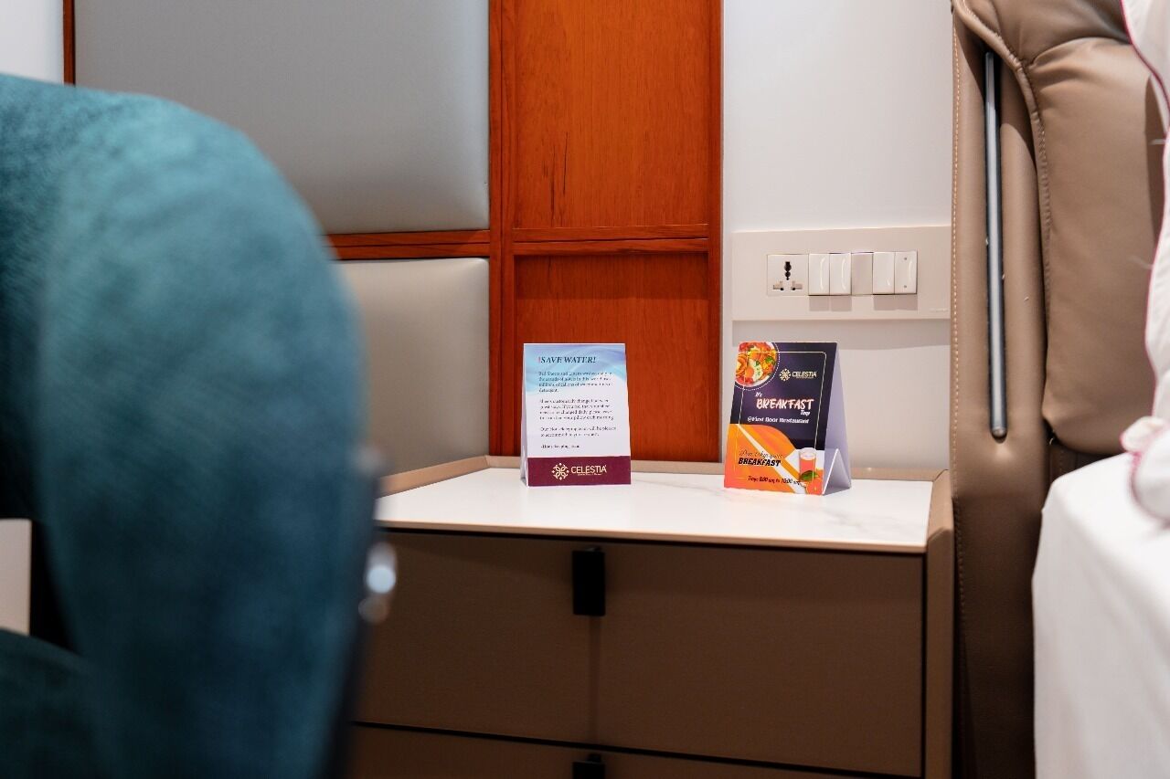 Quarto de hotel com parede de painel de madeira, mesa de cabeceira branca, placa promovendo a conservação da água e uma caixa de café da manhã sobre a mesa.