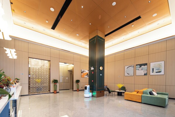 Um hall amplo com balcão de atendimento, área de estar com sofá e poltronas, um robô e um painel vertical grande com controles.