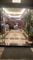 Entrada de hotel com balcão de recepção, área de estar e placa indicando a entrada.