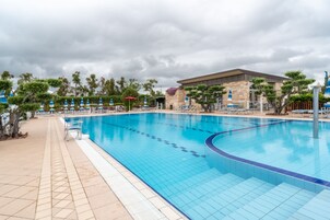 Uma piscina com um deck revestido, uma área coberta com assentos e um edifício com paredes de pedra e telhado plano.