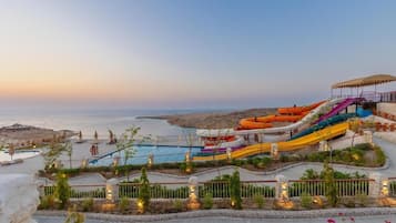Um parque aquático com vários toboáguas, uma piscina e vista para o oceano.