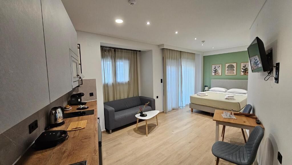 Quarto de hotel moderno com cozinha compacta, sofá, cama e televisão na parede.
