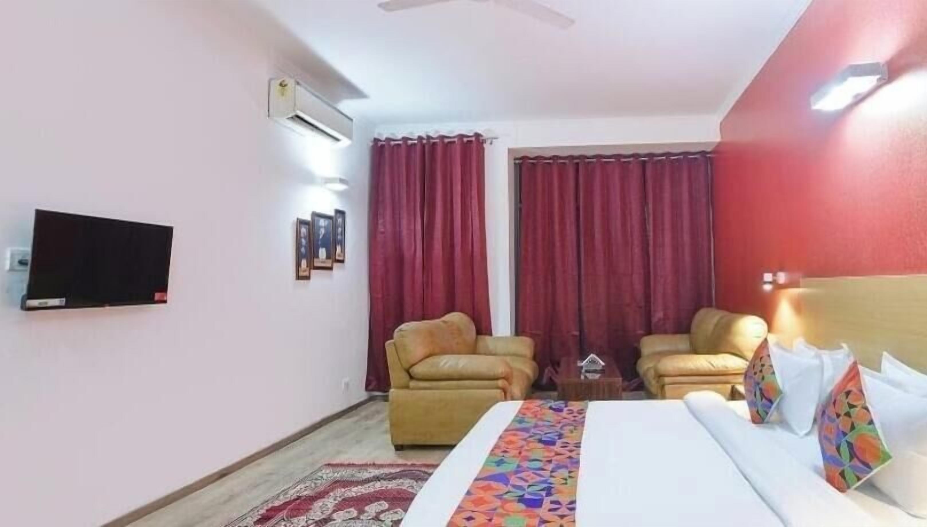 Quarto de hotel com uma cama, duas poltronas, uma televisão e cortinas vermelhas.