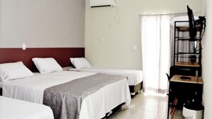 Quarto de hotel com três camas, uma escrivaninha e um ar condicionado.