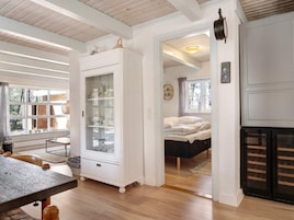Quarto com piso de madeira, um armário branco com portas de vidro, uma cama com roupa de cama branca e uma lareira.