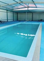 Piscina interior com chão em azulejo e teto de vidro.