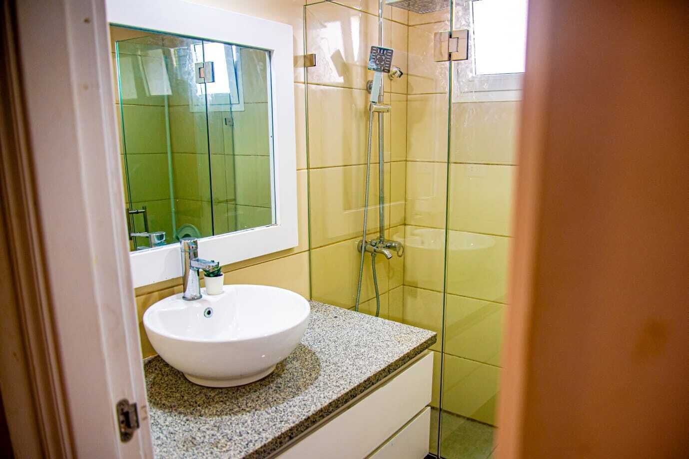 Um banheiro com pia branca, box de vidro e paredes azulejadas em amarelo.