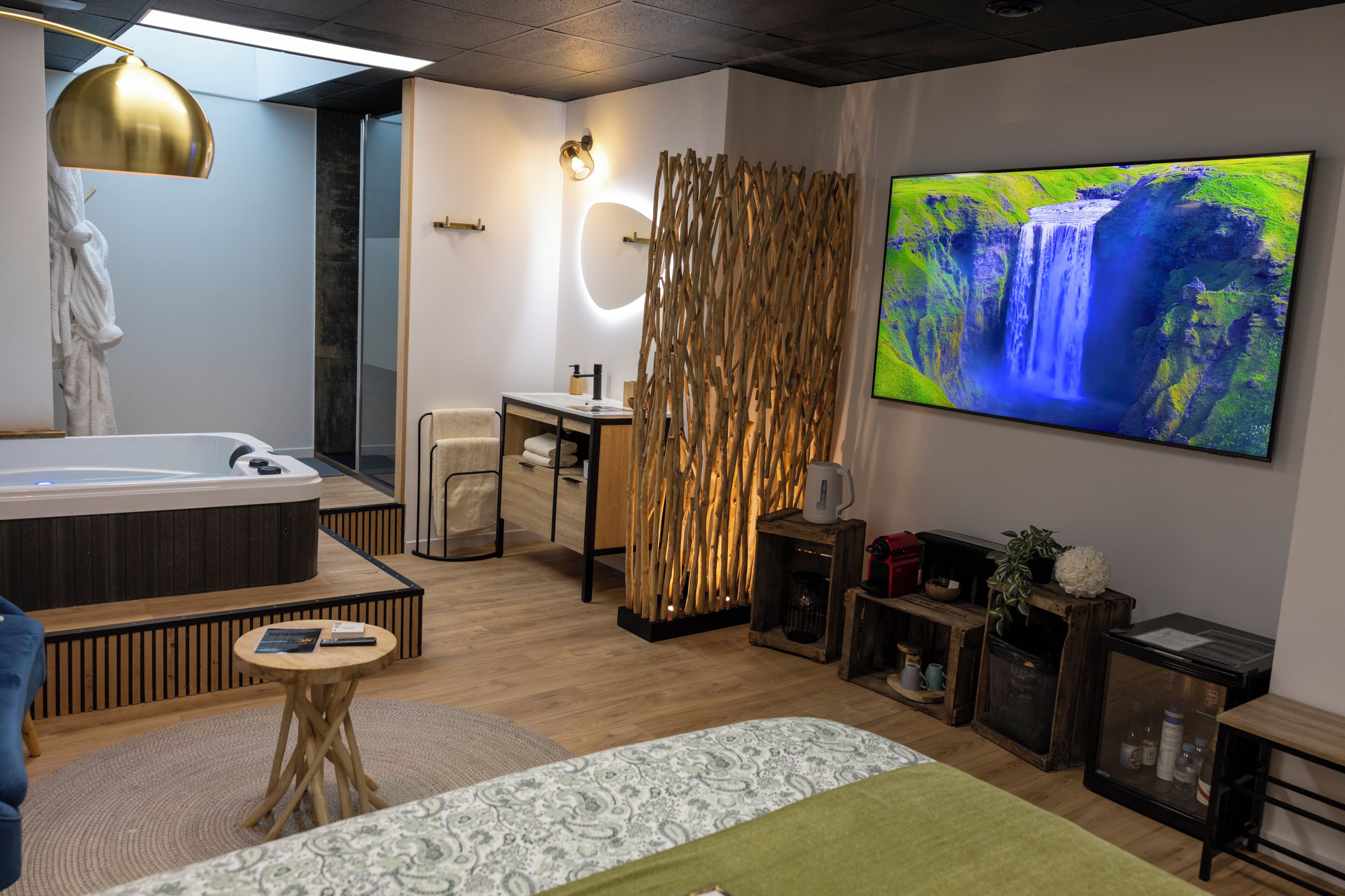 Um spa moderno com uma banheira grande, uma mesa de escritório, uma cadeira, uma TV exibindo uma cachoeira e um painel de parede em madeira.