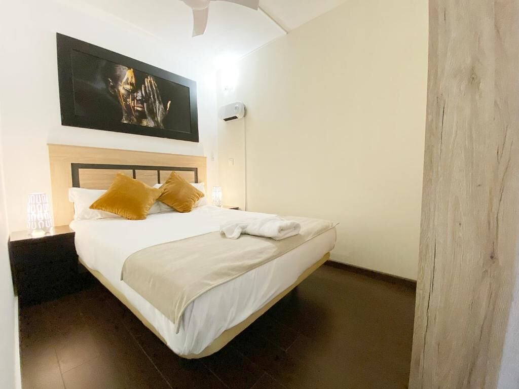 Cama bem arrumada com lençóis brancos e duas almofadas, uma obra de arte na parede acima e piso de madeira.