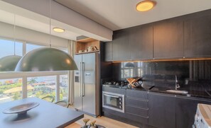 Uma cozinha moderna com armários escuros, eletrodomésticos de aço inoxidável e iluminação pendente.