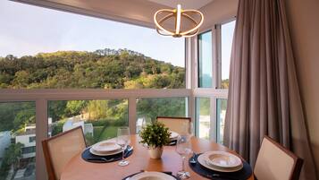Uma área de refeições com uma mesa posta para dois, um candelabro e vista para uma colina arborizada.