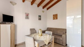 Uma sala de estar moderna com teto de madeira, sofá, mesa de jantar com cadeiras e TV sobre um móvel.