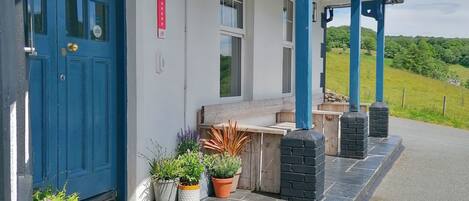 Um edifício com porta azul, placa de boas-vindas e vasos de plantas no alpendre.