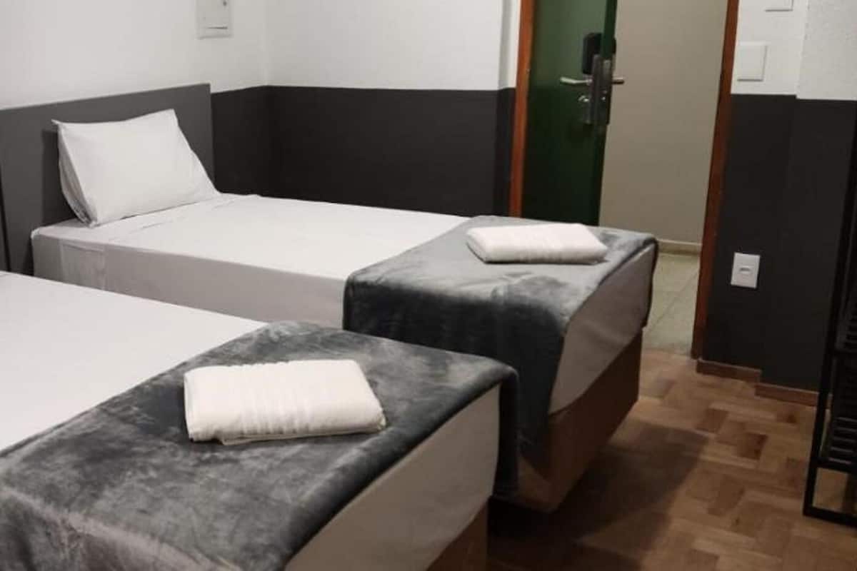 Quarto com duas camas de solteiro, cada uma com uma almofada e uma toalha dobrada.