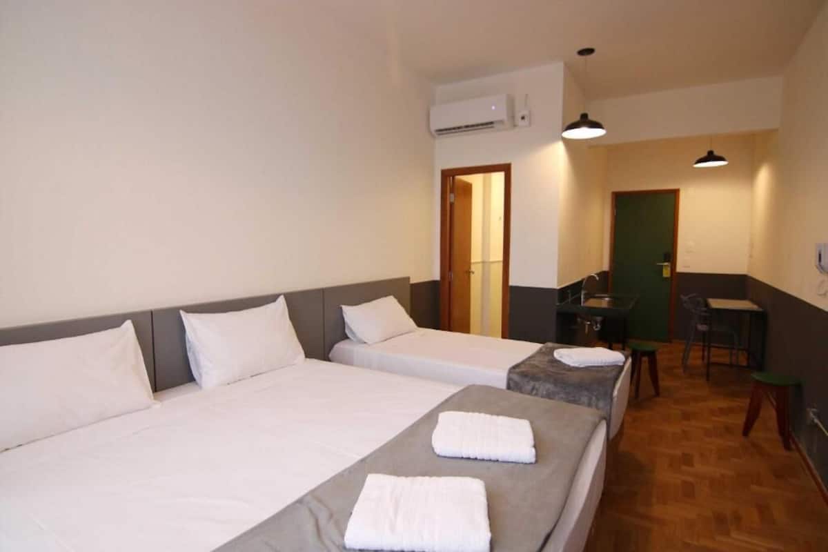 Quarto de hotel com duas camas, uma escrivaninha e uma cadeira.