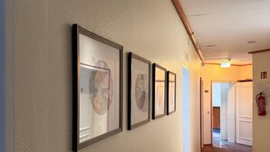 Um corredor com quadros nas paredes, piso de madeira e área carpetada que leva a uma porta aberta.