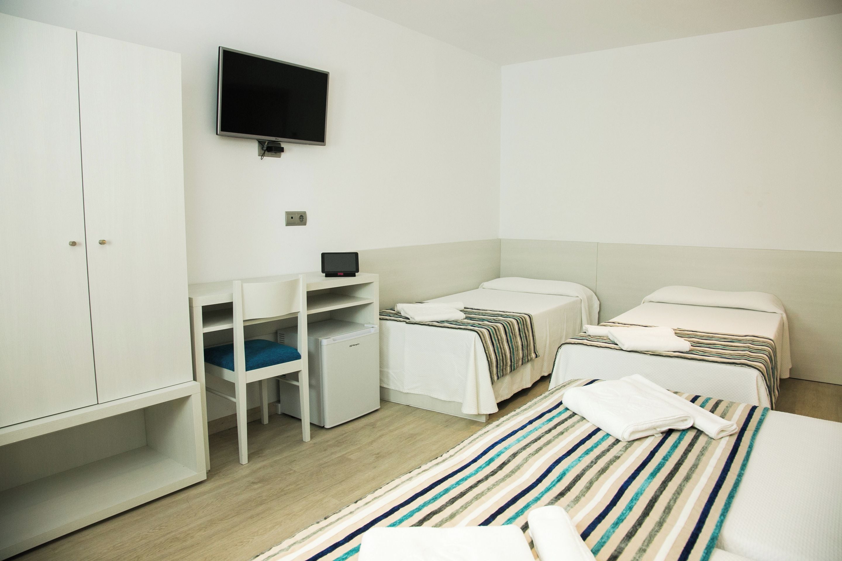 Quarto de hotel com cama, escrivaninha, cadeira, televisão e guarda-roupa.