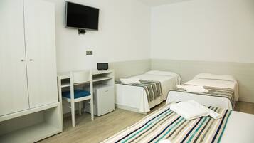 Quarto de hotel com cama, escrivaninha, cadeira, televisão e guarda-roupa.