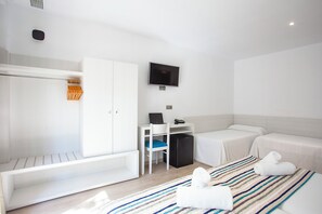 Quarto de hotel com cama, escrivaninha com computador, televisão e armário.