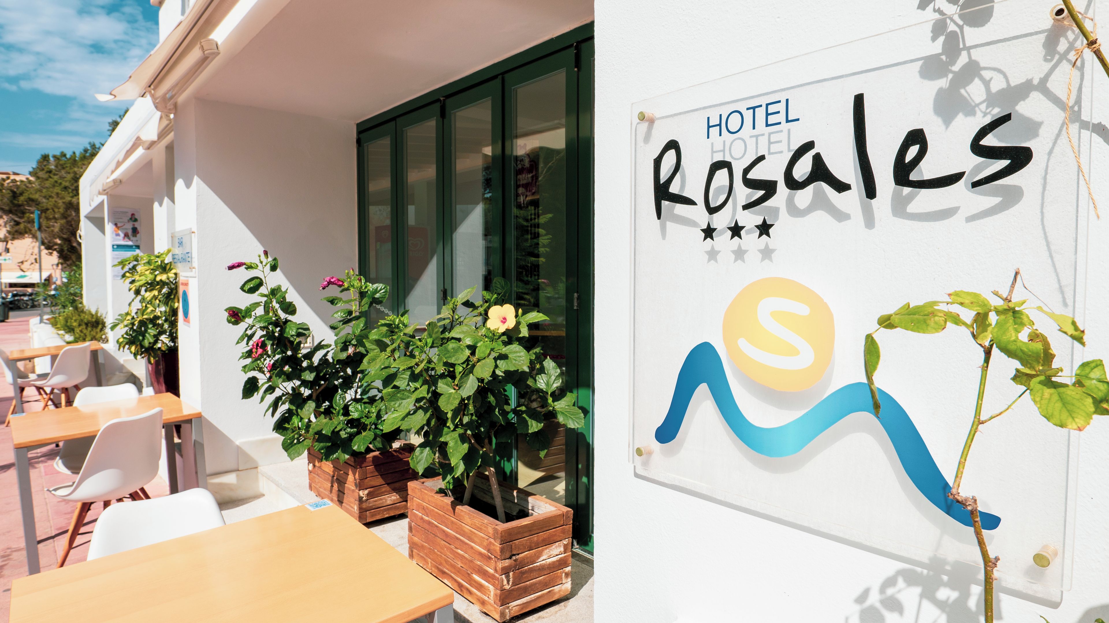 Exterior de hotel com área de estar ao ar livre, plantas em vasos e uma placa com o nome do hotel.