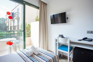 Quarto de hotel com cama, escrivaninha, cadeira, televisão e varanda com mesa e cadeiras.
