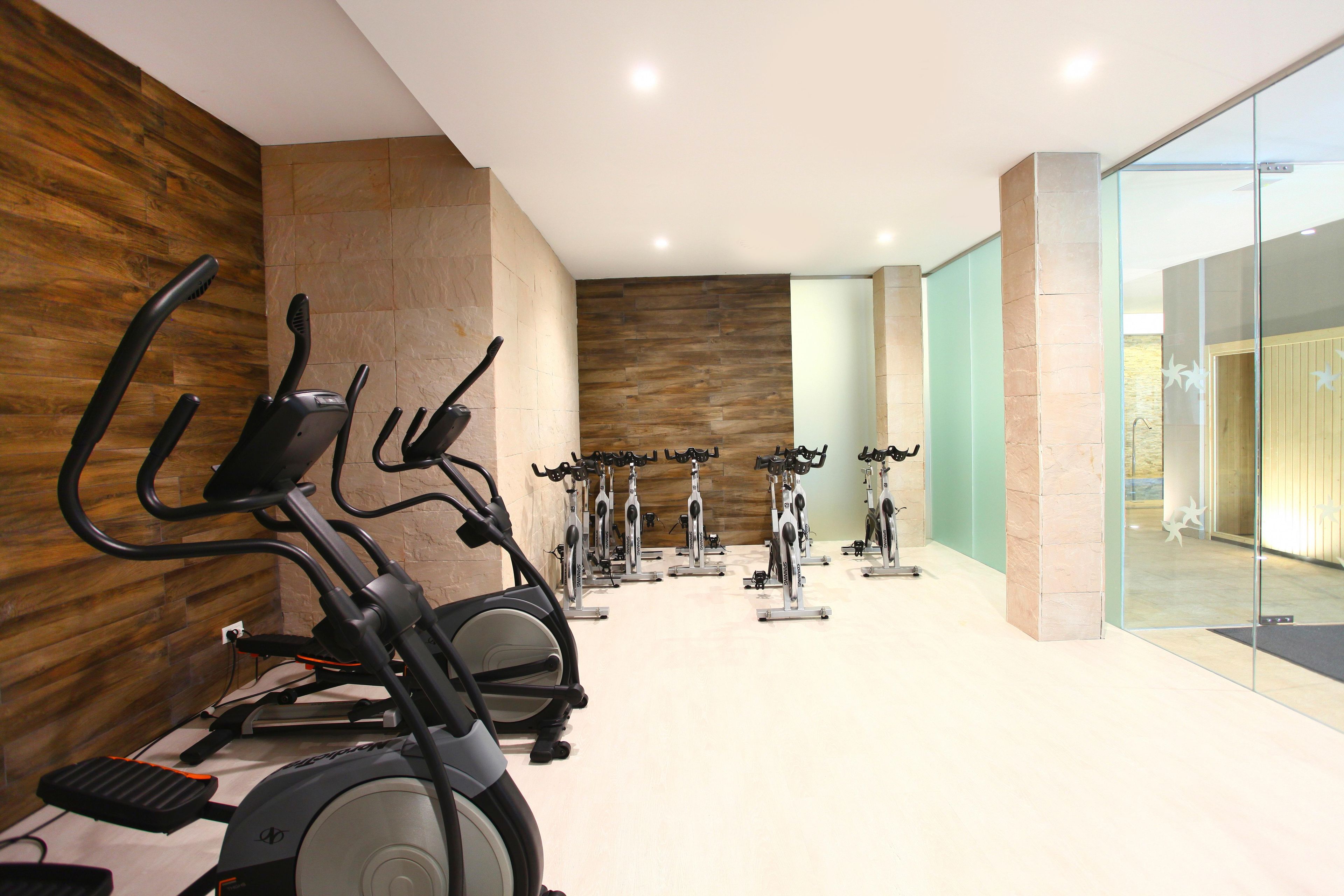 Uma academia moderna com bicicletas ergométricas e elípticos, paredes de madeira e uma porta de vidro que dá para um ambiente claro.