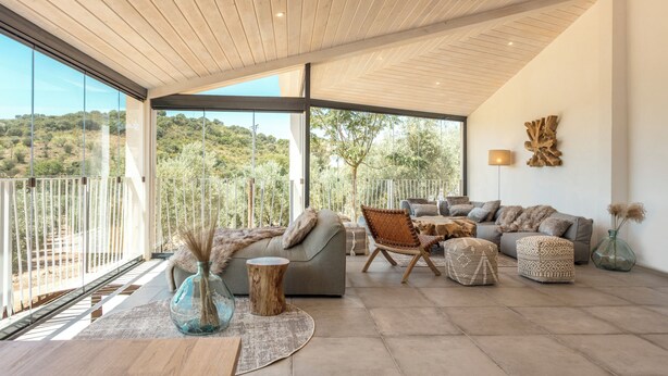 Ampla sala de estar com uma grande janela que oferece vista para o exterior, design de teto moderno e um confortável conjunto de assentos.
