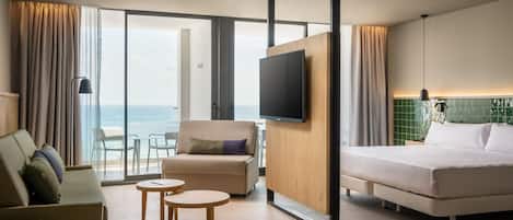 Quarto de hotel com cama, sofá, televisão, mesinha e varanda vista para o mar.