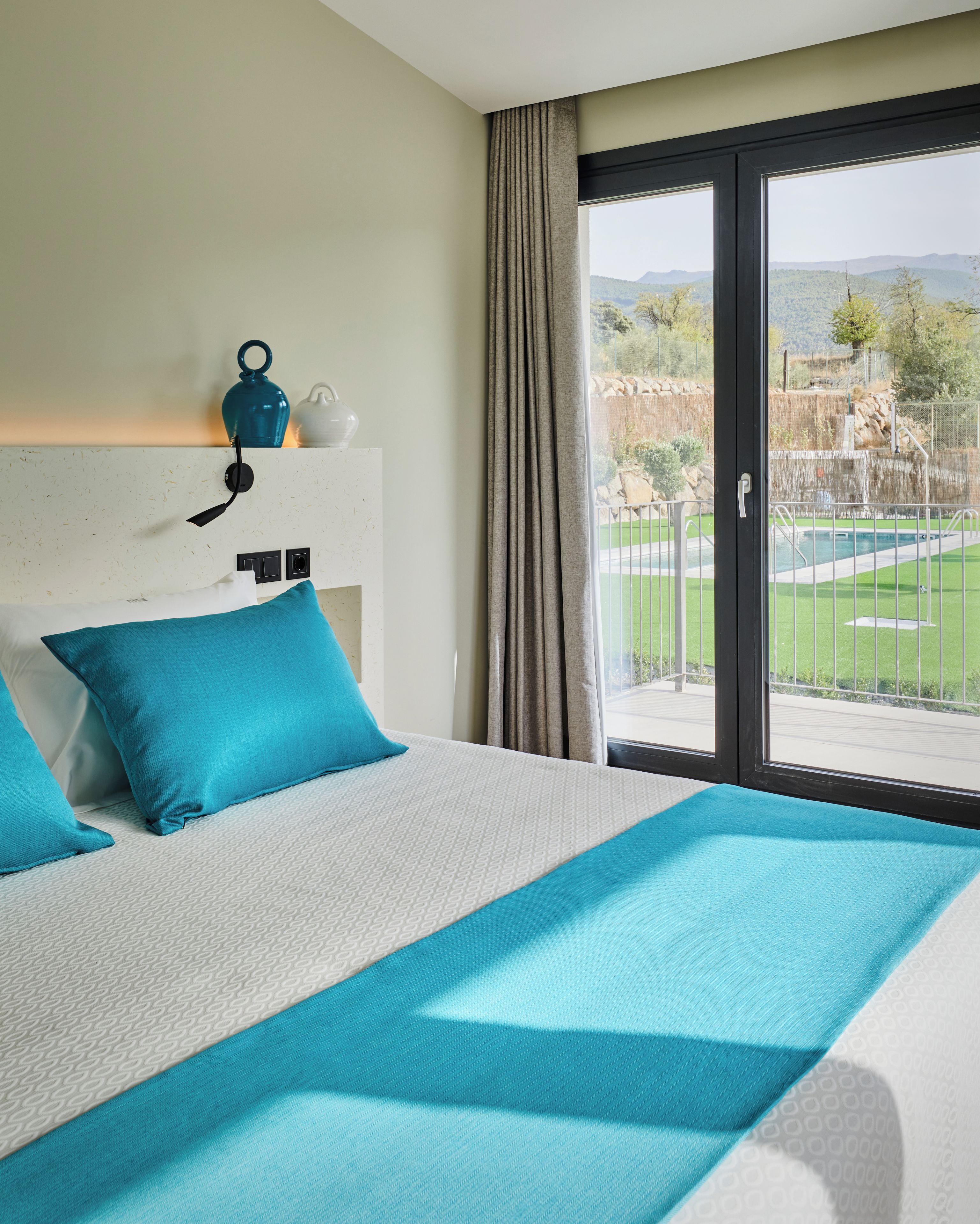 Quarto de hotel com uma cama grande, vista para uma piscina e montanhas, e uma janela com cortinas.