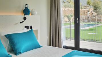 Quarto de hotel com uma cama grande, vista para uma piscina e montanhas, e uma janela com cortinas.