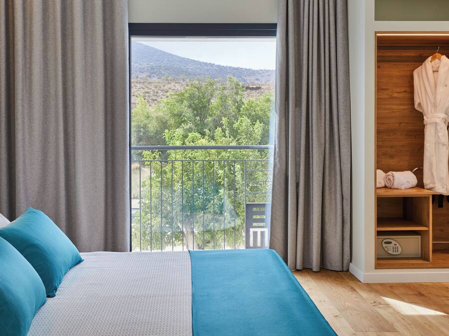 Quarto com cama, guarda-roupa e varanda com vista para árvores e colinas.