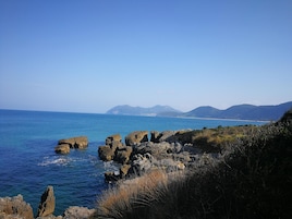 Paisagem costeira com afloramentos rochosos e vista clara do mar e montanhas ao longe.